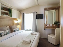 Quarto de hotel com cama, uma cadeira, televisão e espelho.