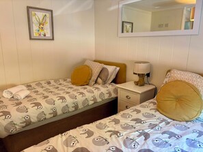 Quarto com duas camas, cada uma com um design de almofada único, uma mesa de cabeceira com luminária e um quadro na parede.