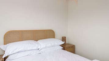 Uma cama com roupa de cama branca, cabeceira de vime e mesa de cabeceira com abajur.