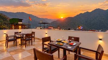 Área de refeições no terraço com vista para o pôr do sol e montanhas.