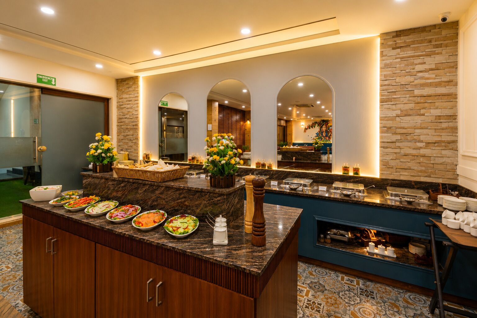 Espaço de café da manhã de hotel, com balcão de mármore, diversos alimentos e um espelho refletindo o ambiente.