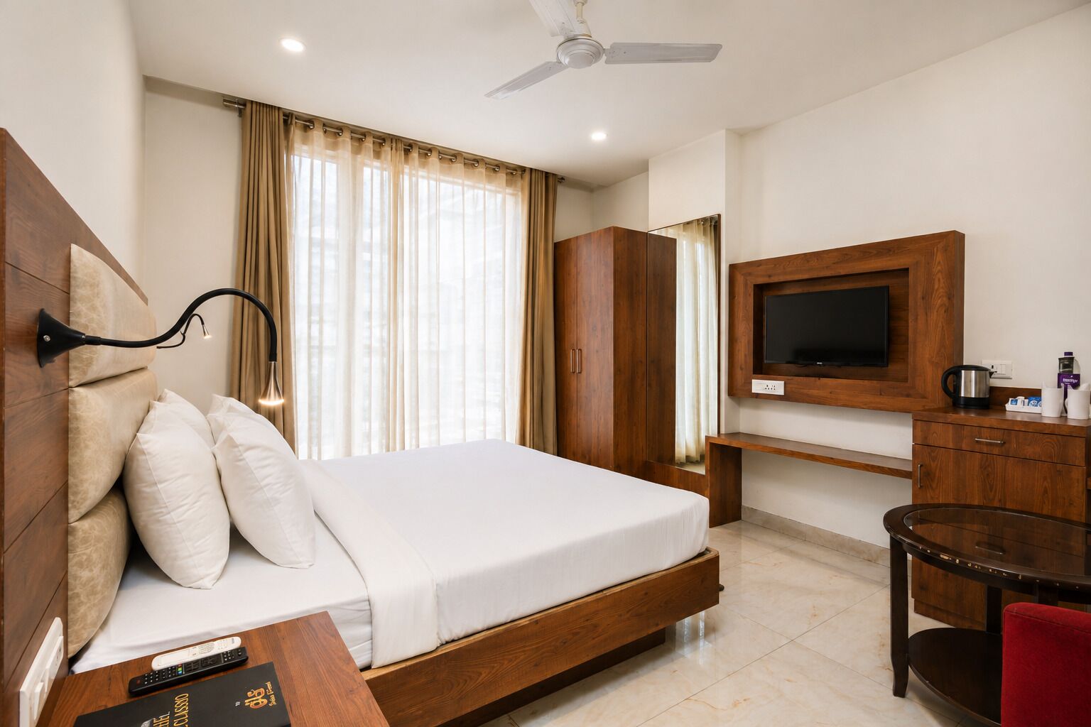 Quarto de hotel com cama, televisão, escrivaninha e guarda-roupa.