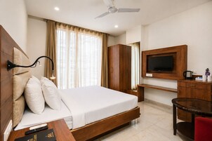 Quarto de hotel com cama, televisão, escrivaninha e guarda-roupa.