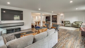 Uma sala de estar moderna com televisão de tela plana, sofás cinzas, uma mesa de centro e uma área de jantar ao fundo.