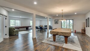 Uma sala de estar ampla com mesa de bilhar, sofá e uma grande janela com vista para o exterior.
