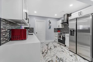 Uma cozinha moderna com geladeira de aço inoxidável, um eletrodoméstico vermelho e um forno preto.