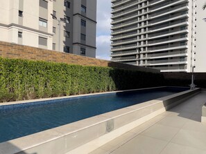 Uma piscina com borda revestida, rodeada por um muro de tijolos e um sequeiro.