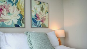 Quarto de hotel com uma cama, um abajur e dois quadros florais na parede.