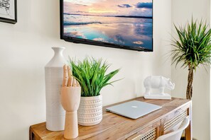 Uma mesa de madeira com um laptop, um vaso branco, uma planta em vaso e uma escultura branca.