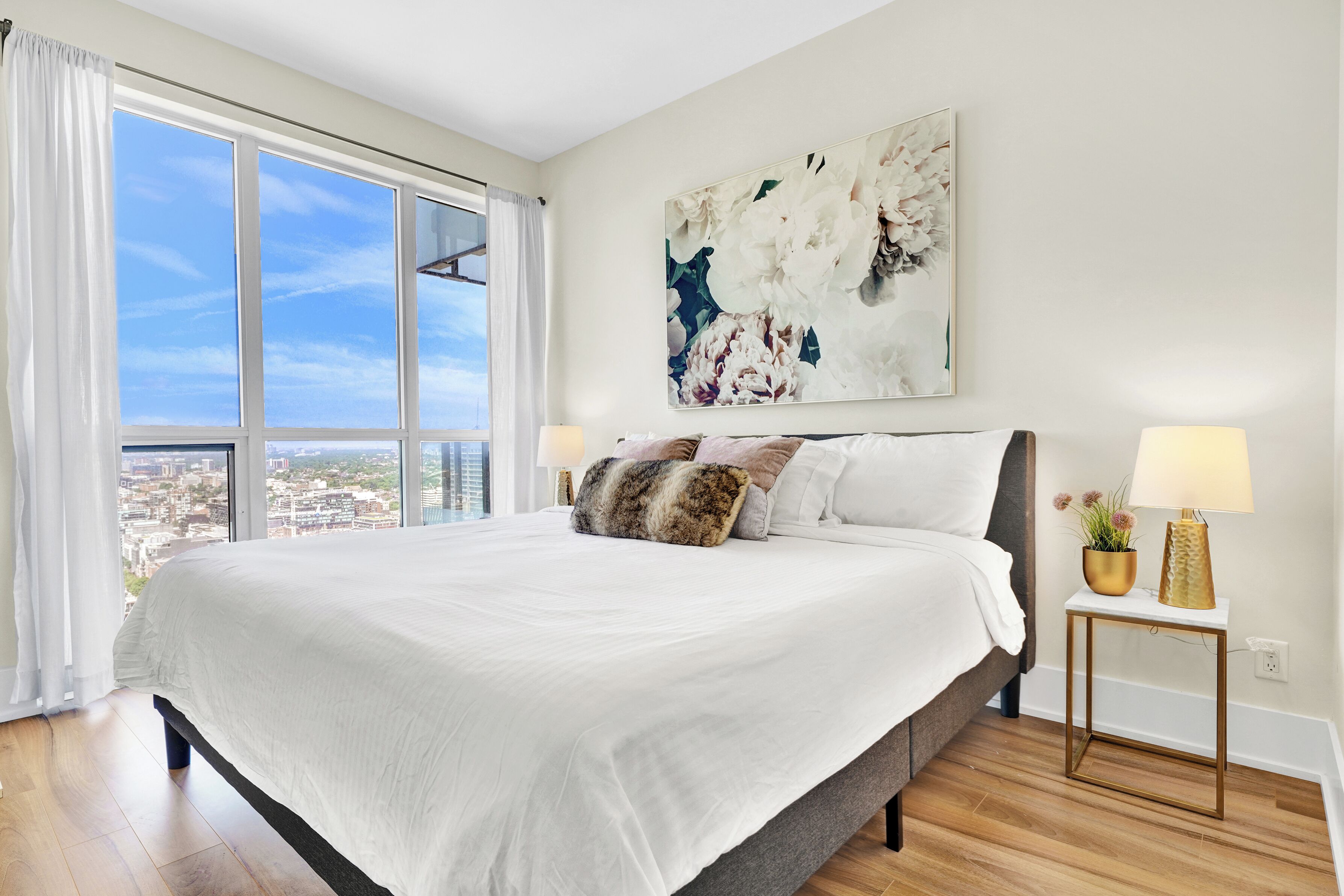 Quarto moderno com cama grande, vista da cidade e um quadro decorativo.