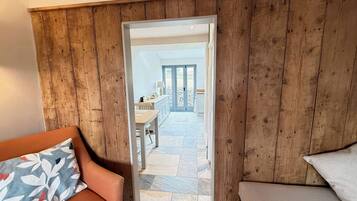 Um quarto com parede de madeira, um sofá, uma cadeira e uma porta que dá para uma área de jantar.