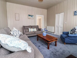 Uma sala de estar com um sofá, uma poltrona azul, uma mesa de centro de madeira e um vaso com flores.