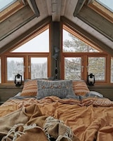 Um quarto acolhedor com teto inclinado, grandes janelas e cama com roupa de cama estampada.