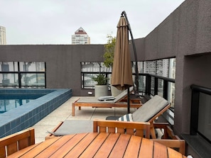 Terraço no telhado com piscina, espreguiçadeiras e um vaso de planta.