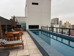 Área de piscina no terraço com espaço para sentar e vista panorâmica da cidade.