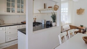 Uma cozinha moderna com armários brancos, bancada preta e um espaço de refeições com mesa e cadeiras brancas.