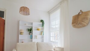 Uma sala de estar moderna com um sofá, uma poltrona de vime, uma mesa de madeira, uma tigela verde e uma estante branca com diversos objetos.
