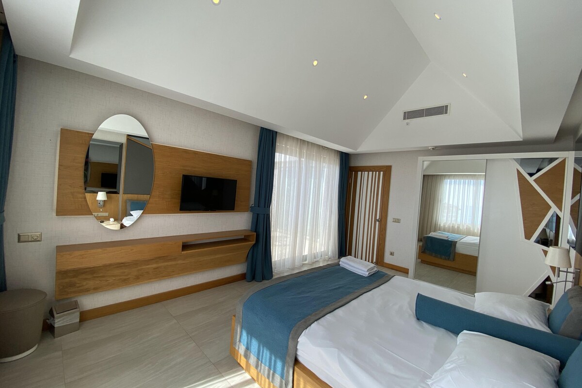 Quarto de hotel moderno com uma cama grande, televisão na parede, espelho e guarda-roupa.