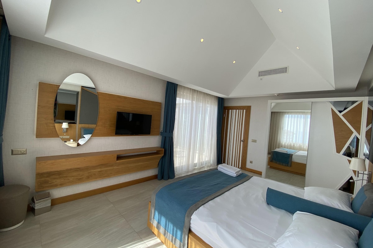 Quarto de hotel moderno com uma cama grande, televisão na parede, espelho e guarda-roupa.