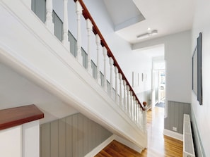 Uma escadaria com balaústres brancos e corrimão de madeira, que leva a um quarto com radiador e porta para o exterior.
