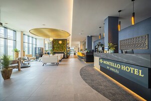 Uma área de recepção de hotel com design moderno, incluindo um balcão de atendimento, área de estar e uma parede grande com padrão geométrico.