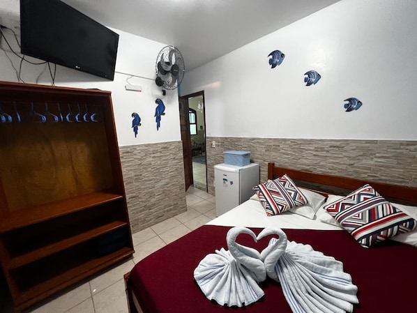 Quarto de hotel com cama, guarda-roupa de madeira, televisão, ventoinha na parede e decoração de peixes na parede.