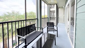 Varanda com duas cadeiras pretas e uma mesa, ventoinha no teto e vista para o verde.