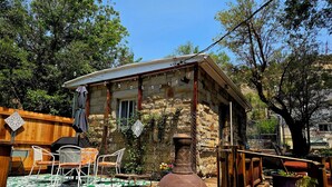 Um edifício rústico de pedra com um deck de madeira, área de estar externa e uma churrasqueira de metal.