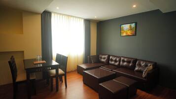 Sala de estar com sofá de couro marrom, mesa de centro, mesa de jantar com cadeiras e um quadro na parede.