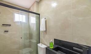 Uma casa de banho moderna com cabine de chuveiro em vidro, sanita e lavatório com bancada preta.