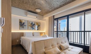 Quarto de hotel com cama, sofá, janela ampla com vista e obras de arte na parede.