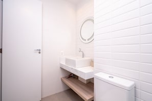 Casa de banho com uma sanita, uma pia branca e um espelho.