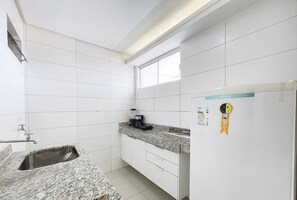 Uma cozinha com azulejos brancos, uma pia, bancada com cafeteira e armários.