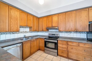 Cozinha com armários de madeira, lava-louças de aço inoxidável, forno duplo e painel de azulejos.