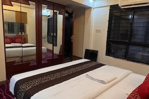 Quarto de hotel com cama, espelho, guarda-roupa e janela com persianas.