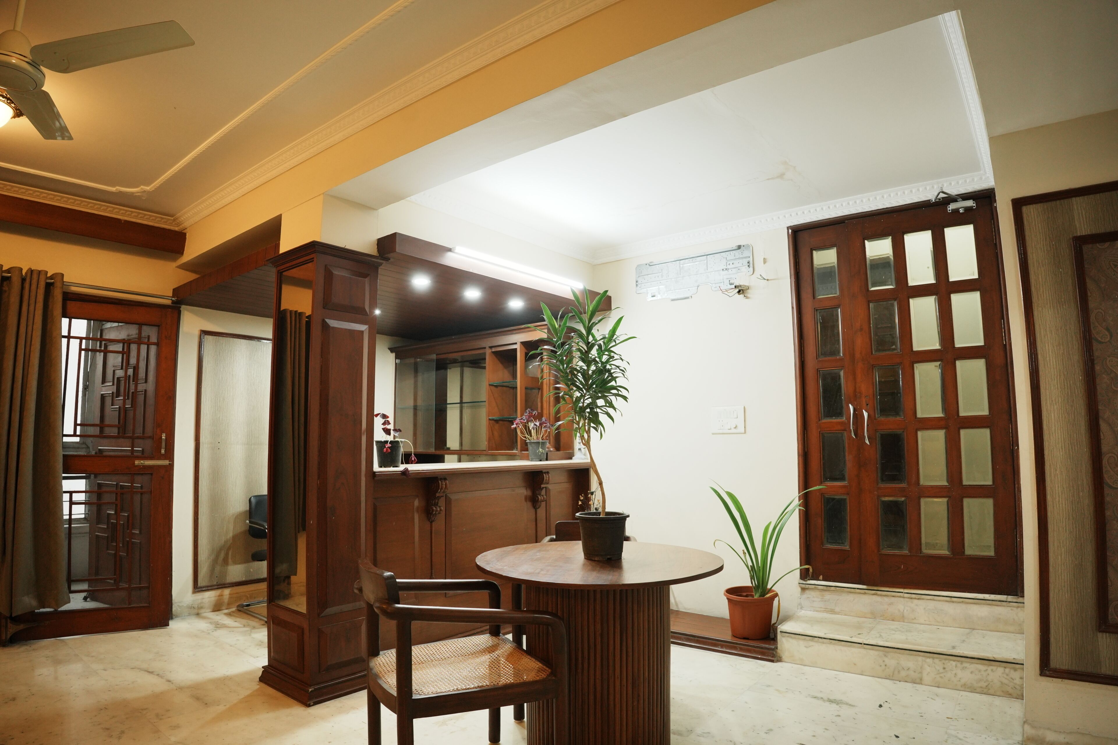 A room with a dining table, chairs, a potted plant, a mirror, and a wooden door.
