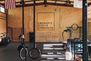 Uma academia com parede de madeira, equipamentos de ginástica e uma placa com a inscrição 'CROSSFIT OTOTOY STRENGTH'.