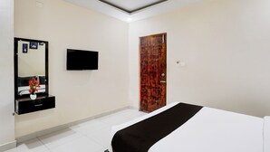 Quarto de hotel com uma cama, televisão de tela plana na parede, porta de madeira e um espaço pequeno para o banheiro.