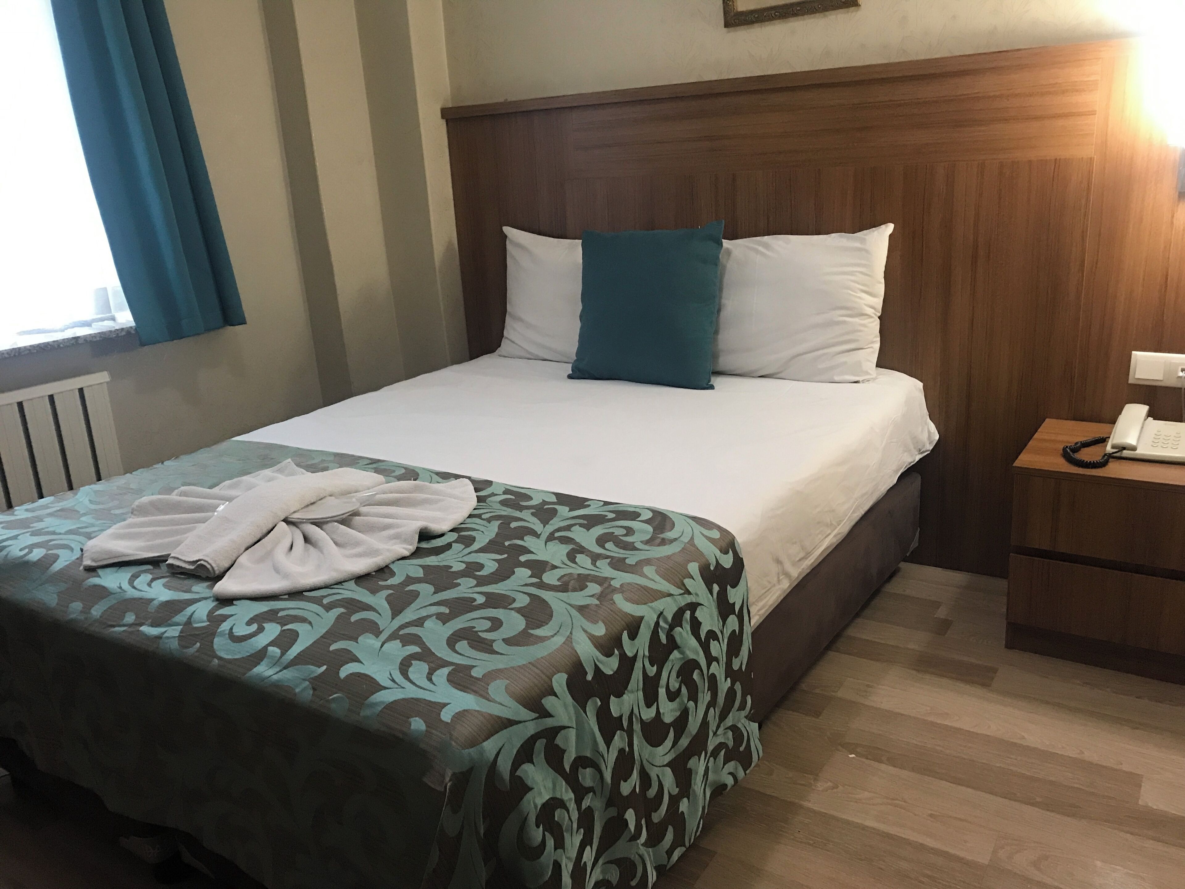 Quarto de hotel com uma cama, uma mesa de cabeceira com telefone e uma janela com cortinas.