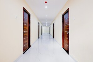 Um corredor com portas de madeira em ambos os lados, chão de azulejos brancos e luminárias embutidas no teto.
