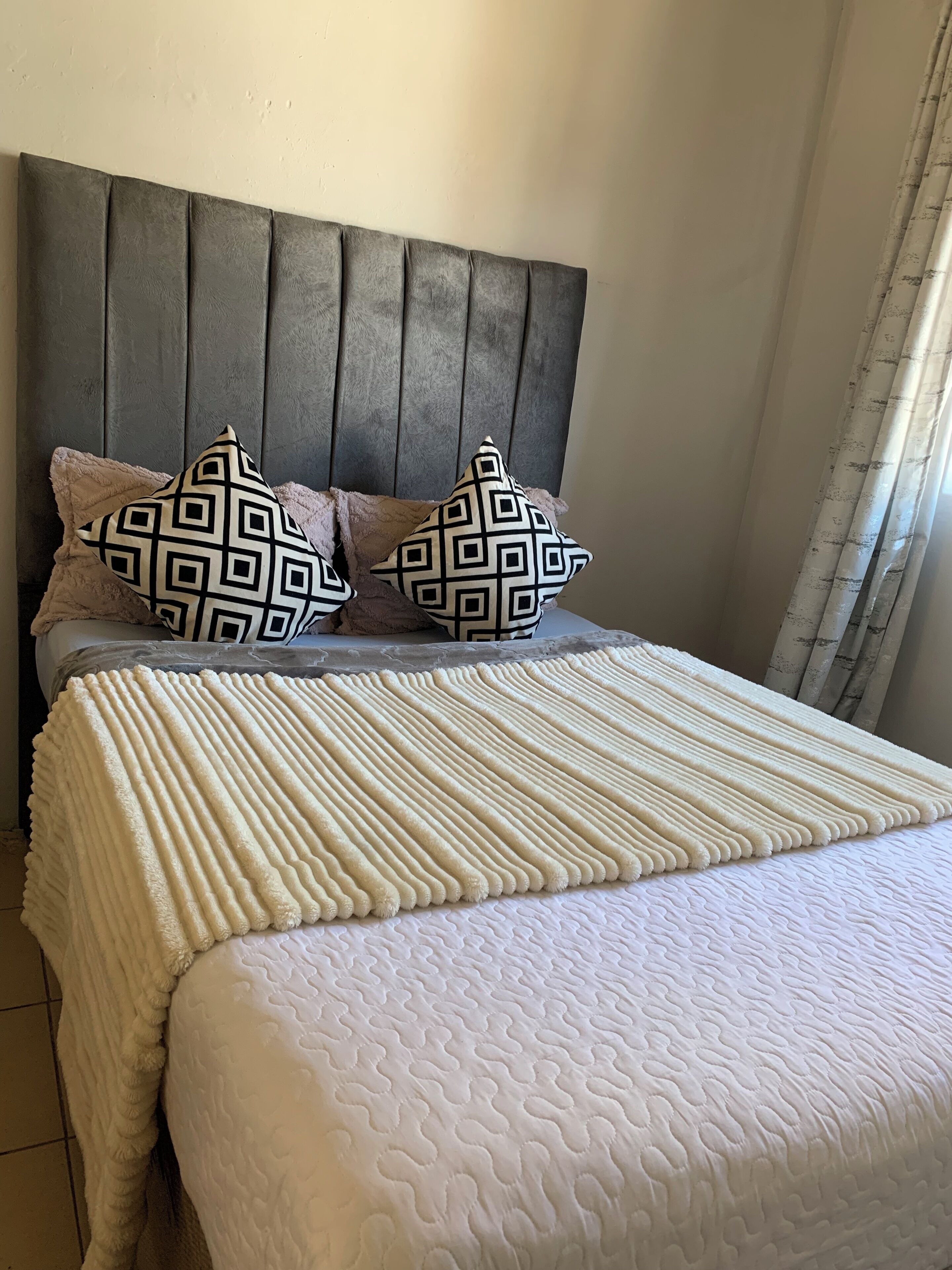 Cama bem arrumada com cabeceira estampada, duas almofadas decorativas e manta texturizada.