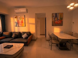 Uma sala de estar com sofá, mesa de centro, mesa de jantar com cadeiras e obras de arte nas paredes.
