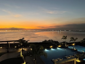Área de piscina com vista para o mar e um pôr do sol.