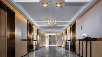 Corredor moderno de hotel com piso de mármore polido, lambris de madeira e um elevador central.