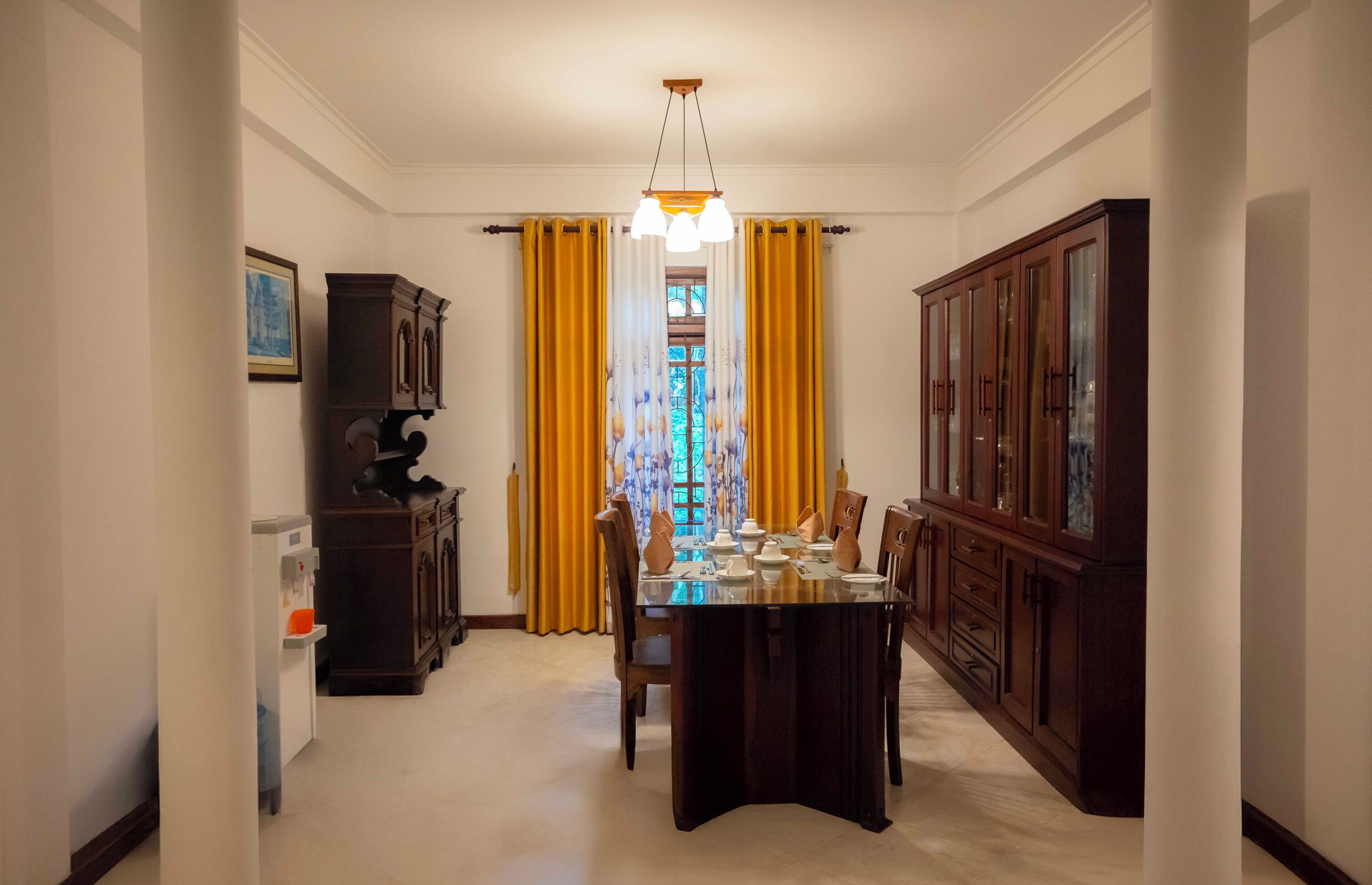 Uma sala de jantar com mesa de vidro, cadeiras de madeira, um candelabro e um armário com portas de vidro.
