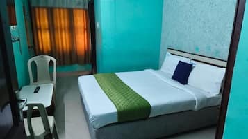 Quarto individual com uma colcha verde, mesa de cabeceira com controle remoto e uma cadeira.