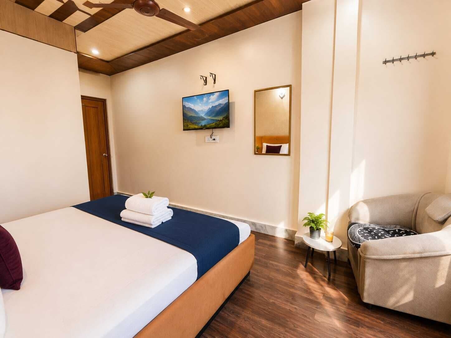 Quarto de hotel com uma cama, uma cadeira, uma mesinha com uma planta, um quadro na parede e um espelho.