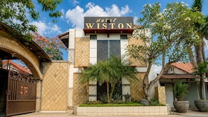 A hotel named 'Hotel WISTON' with a prominent sign, a gated entrance, and a landscaped area with palm trees.