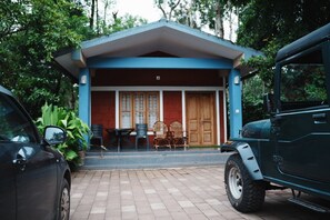 Um edifício com telhado azul, varanda coberta com cadeiras e um carro estacionado na frente.
