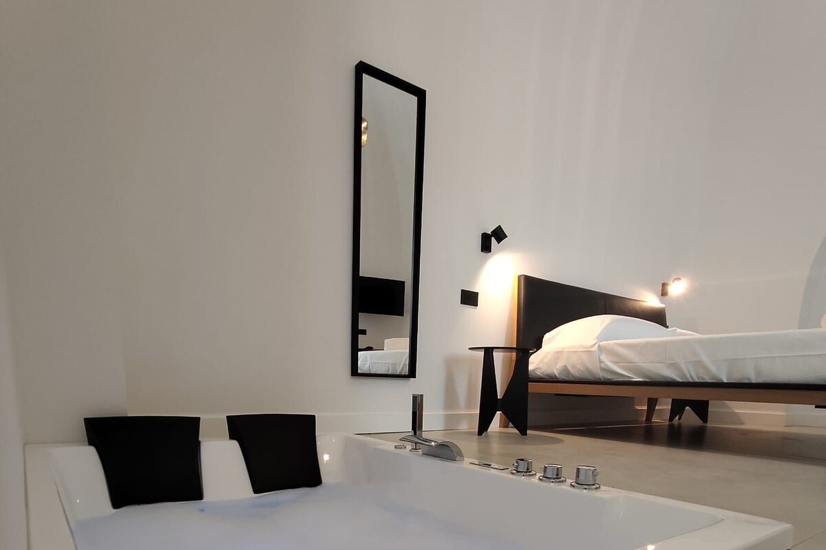 Uma casa de banho moderna com uma banheira grande, um espelho e uma cama ao fundo.